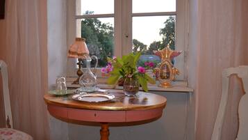 Uma mesa de madeira redonda com um jarro de vidro, um vaso com flores e um abajur decorativo.