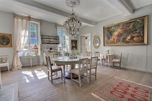 Uma sala de jantar com um lustre, uma pintura grande e uma mesa posta para quatro pessoas.