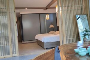 Quarto com cama, luminária de cabeceira, mesa de madeira com objetos decorativos e porta de correr.