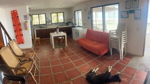 Uma sala de estar com sofá, cadeiras, mesa de jantar e cozinha equipada com frigorífico e fogão.