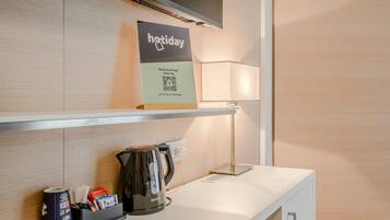 Uma área de recepção de hotel com um letreiro de 'férias', uma chaleira, uma máquina de café e um laptop no balcão.