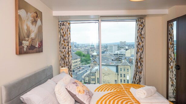Quarto de hotel com uma cama grande, vista para a cidade e um quadro na parede.