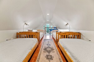 Quarto em dormitório com duas camas de solteiro, cabeceira de madeira, tapete central e vista para o exterior através de uma porta.