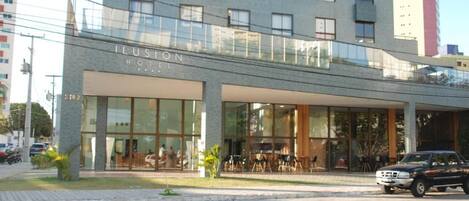 Exterior do Illusion Hotel com fachada moderna, grandes janelas de vidro e área de estar ao ar livre.