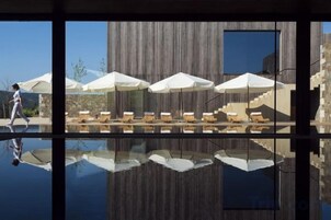 Área de piscina com espreguiçadeiras e guarda-sóis, com reflexos na superfície da água.