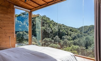 Quarto com uma janela ampla que dá para uma encosta arborizada.