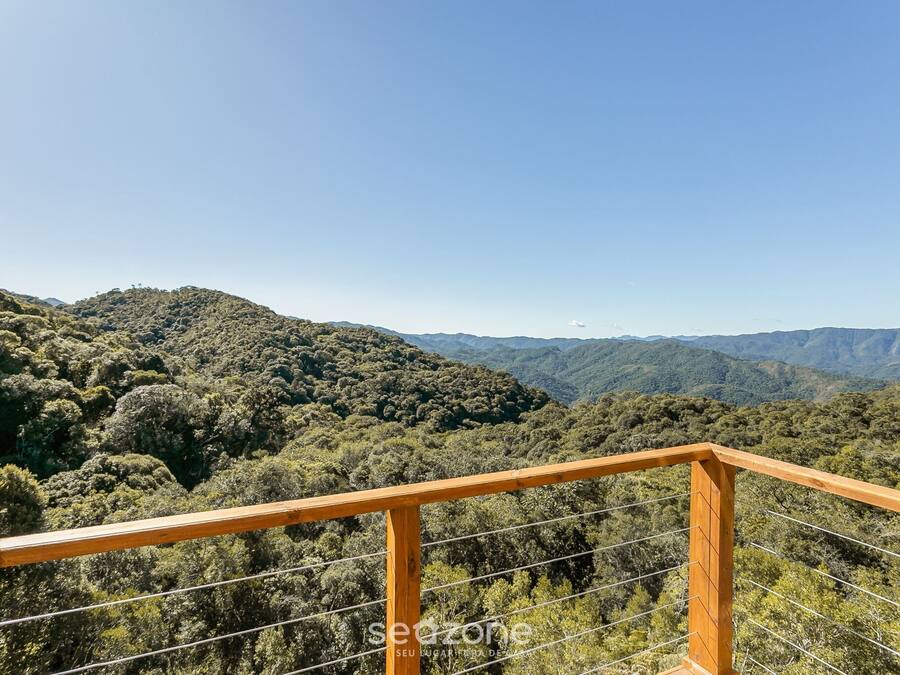 Guarda de varanda de madeira com vista para uma paisagem montanhosa arborizada.