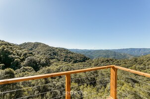 Guarda de varanda de madeira com vista para uma paisagem montanhosa arborizada.