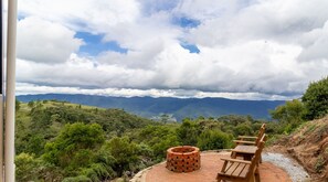 Um pátio com lareira de tijolos e cadeiras de madeira, com vista para uma paisagem montanhosa.