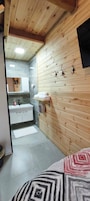 Quarto com teto de madeira, cama com manta estampada, mesa de cabeceira e aquecedor fixado na parede.