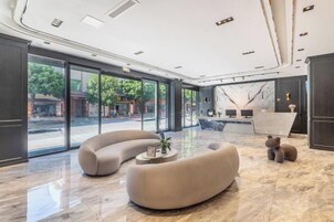 Um saguão moderno com assentos curvos, balcão de recepção e grandes janelas com vista para a rua.