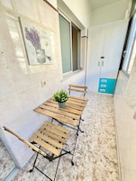 Um pequeno quarto revestido com azulejos, com uma mesa e cadeiras de madeira, um vaso de planta e uma janela.