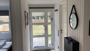Um corredor com porta dupla que dá para área externa, uma cama, um armário preto e um espelho fixado na parede.
