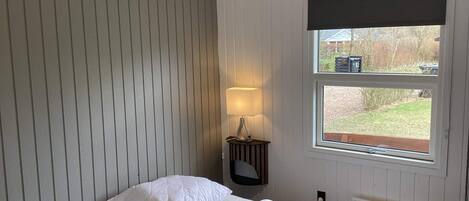 Quarto de hotel com duas camas, uma janela com vista para o exterior e uma luminária de cabeceira.