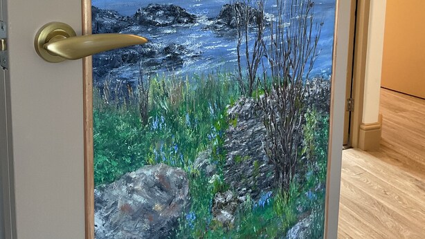 Uma porta com uma pintura de paisagem marinha, um puxador de latão e um chão de madeira.