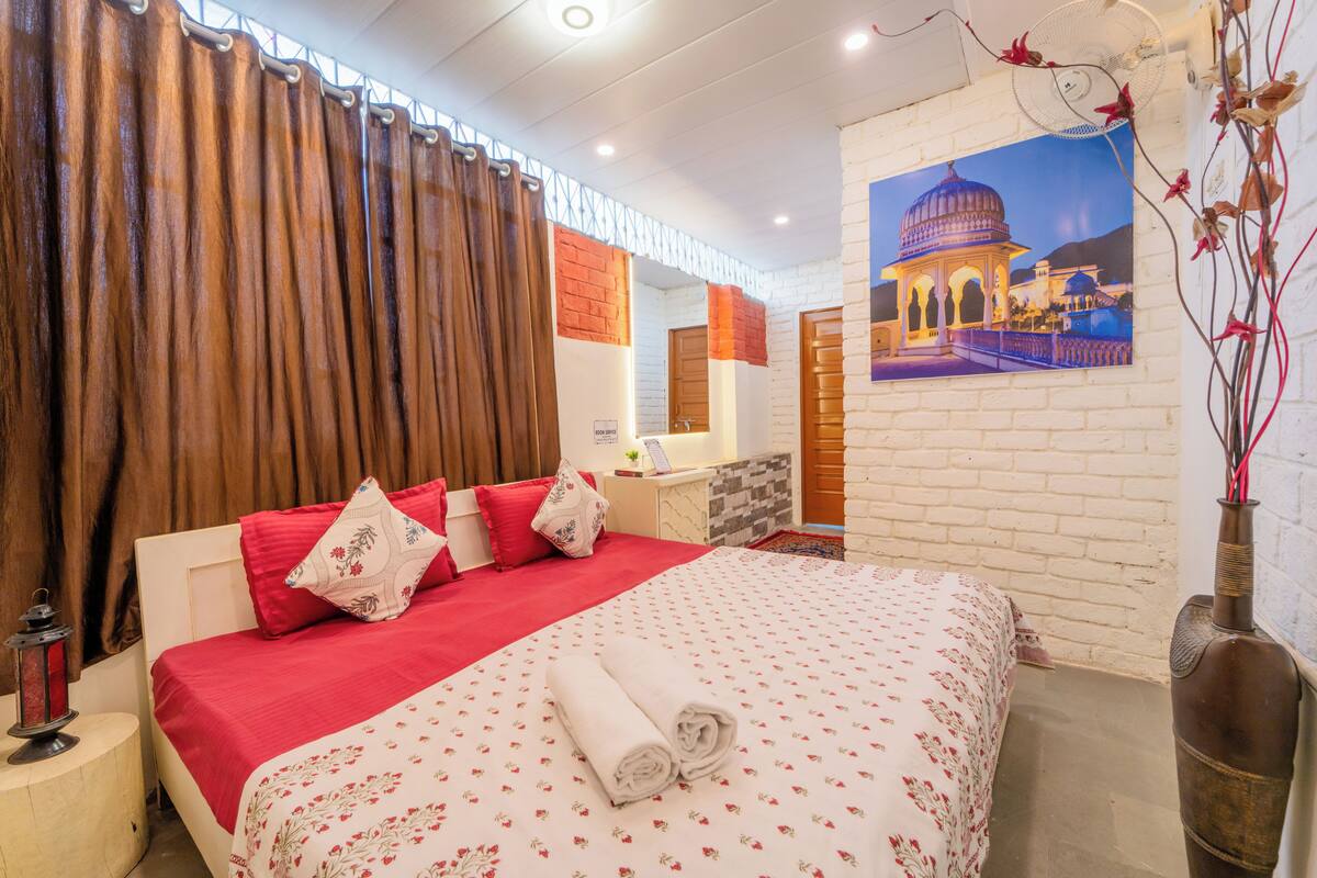Quarto de hotel com cama, mesa de cabeceira, abajur, quadro na parede e um vaso decorativo.