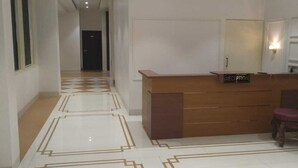 Uma área de recepção com balcão, sala de espera com banco e corredor com piso estampado.