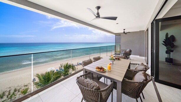 Uma varanda com mesa, cadeiras e vista para a praia.