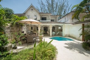 Um edifício de pedra com piscina, área de estar externa e plantas tropicais.
