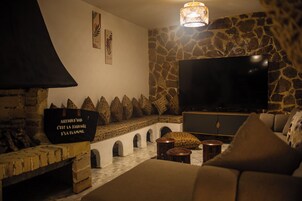 Uma sala de estar aconchegante com uma parede de pedra, uma TV de tela plana, um sofá e um banco com almofadas.