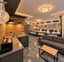 Quarto de hotel moderno com cozinha, sofá, mesa de jantar e uma cama grande com vários travesseiros.