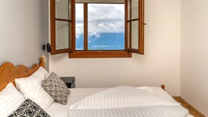 Quarto com cama, almofadas, mesa de cabeceira e janela com persiana aberta.