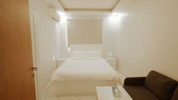 Quarto de hotel com cama, mesas de cabeceira, sofá e uma pequena mesa com um controle remoto.