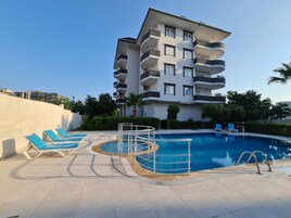 Hotel moderno com piscina no terraço, várias varandas e céu limpo.