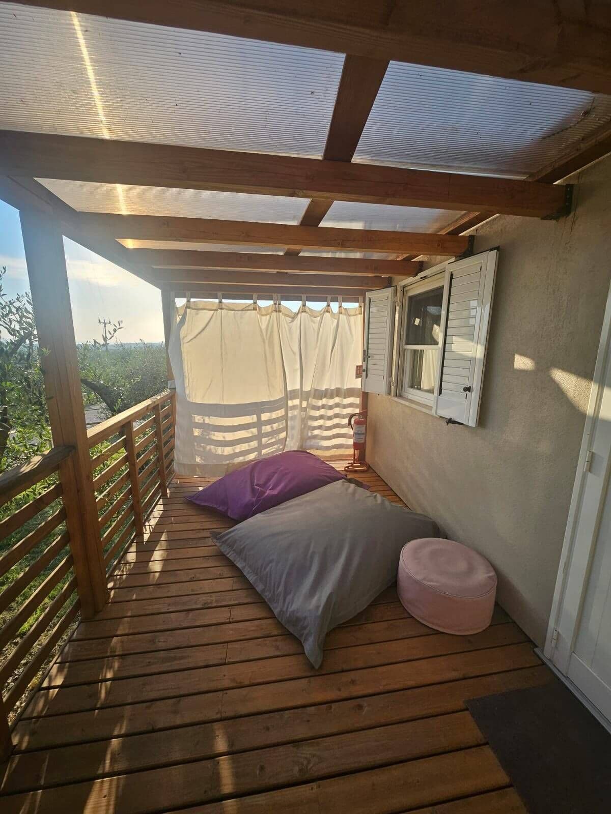 Um deck de madeira com pérgola, uma cama com almofadas, um extintor de incêndio e um quadro fixado na parede.