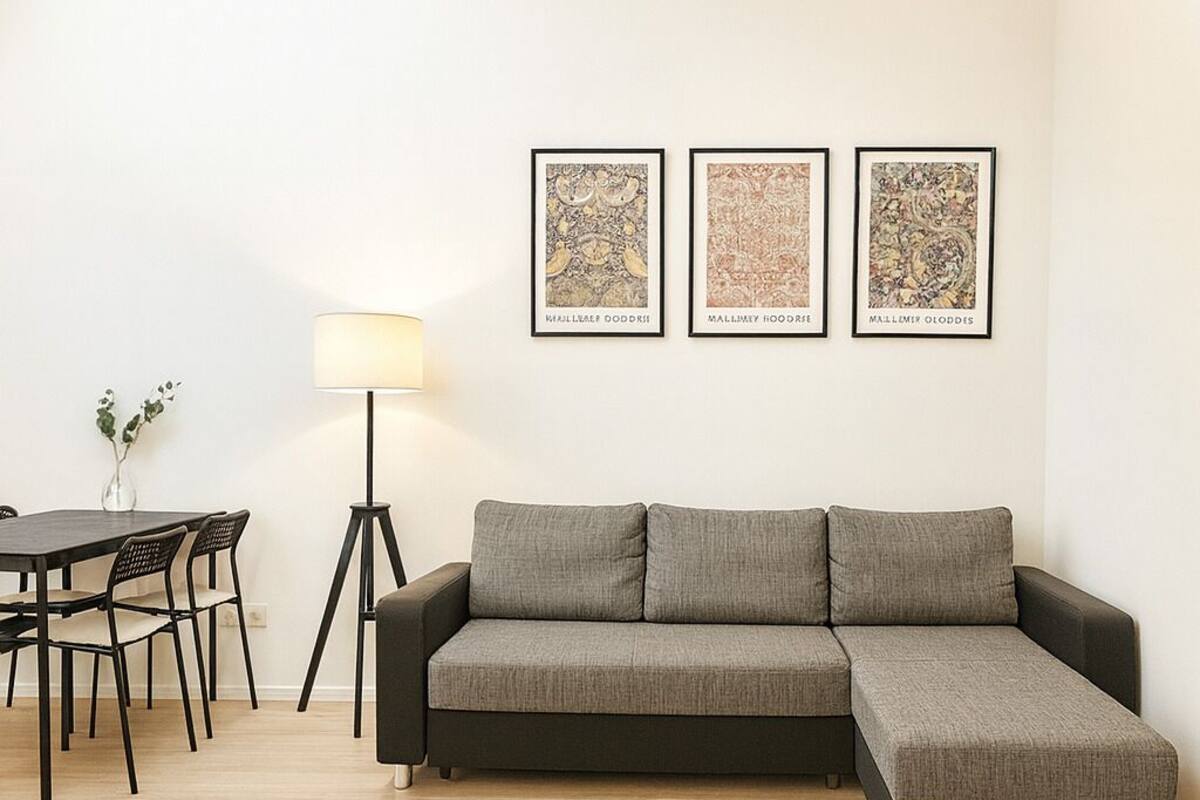 Uma sala de estar moderna com um sofá seccional, uma mesa de jantar com cadeiras, um abajur e três obras de arte emolduradas na parede.