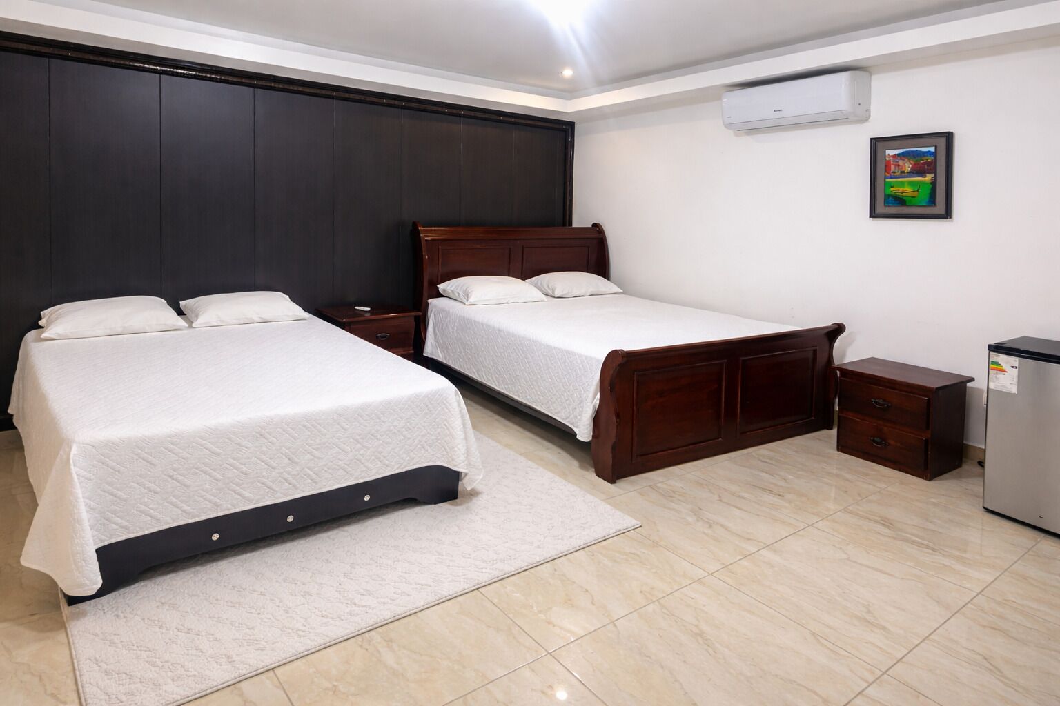 Quarto com duas camas, cómoda, mesa de cabeceira, frigorífico e ar condicionado.