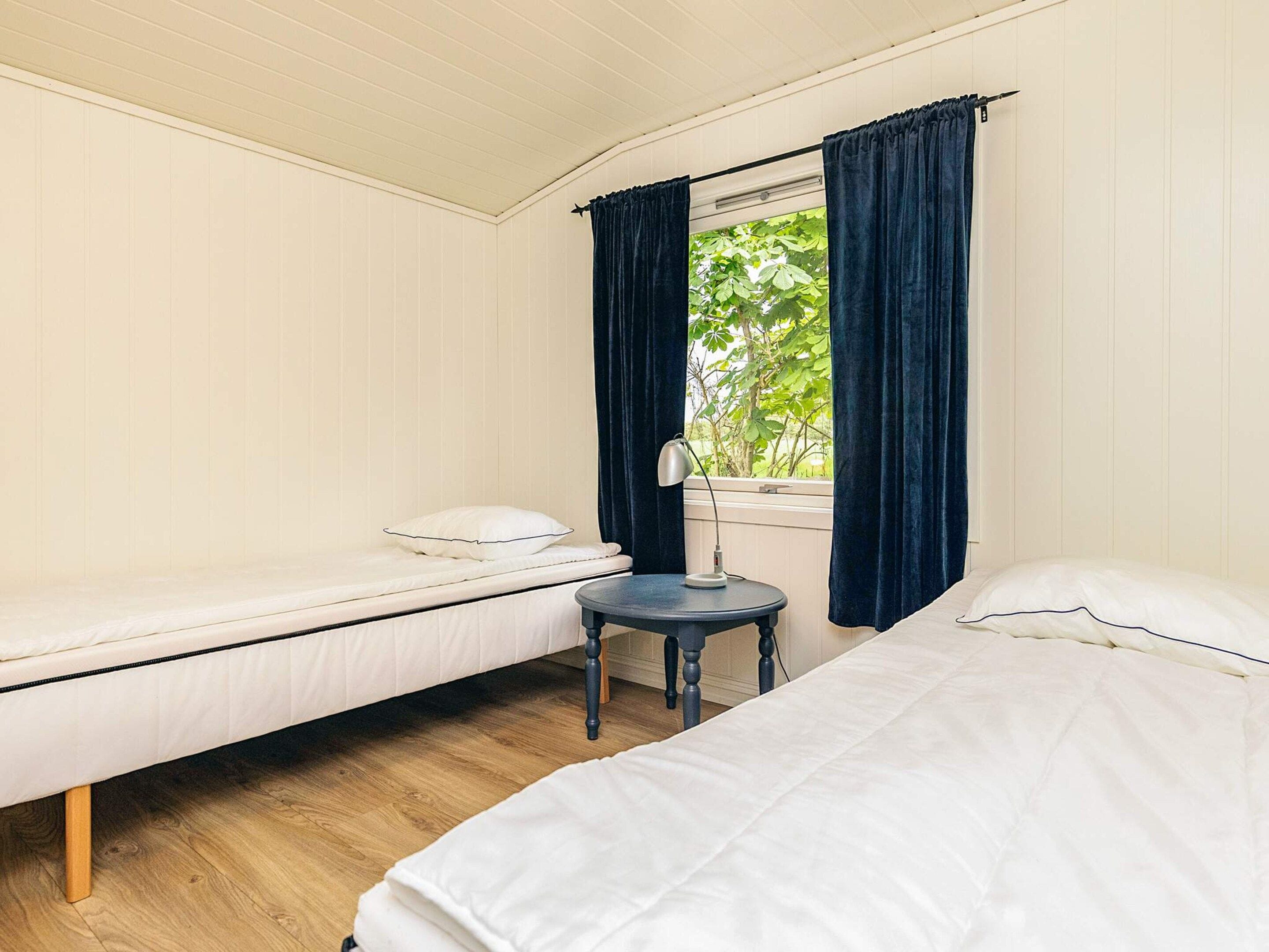 Quarto com duas camas de solteiro, uma mesinha e uma janela com cortinas.