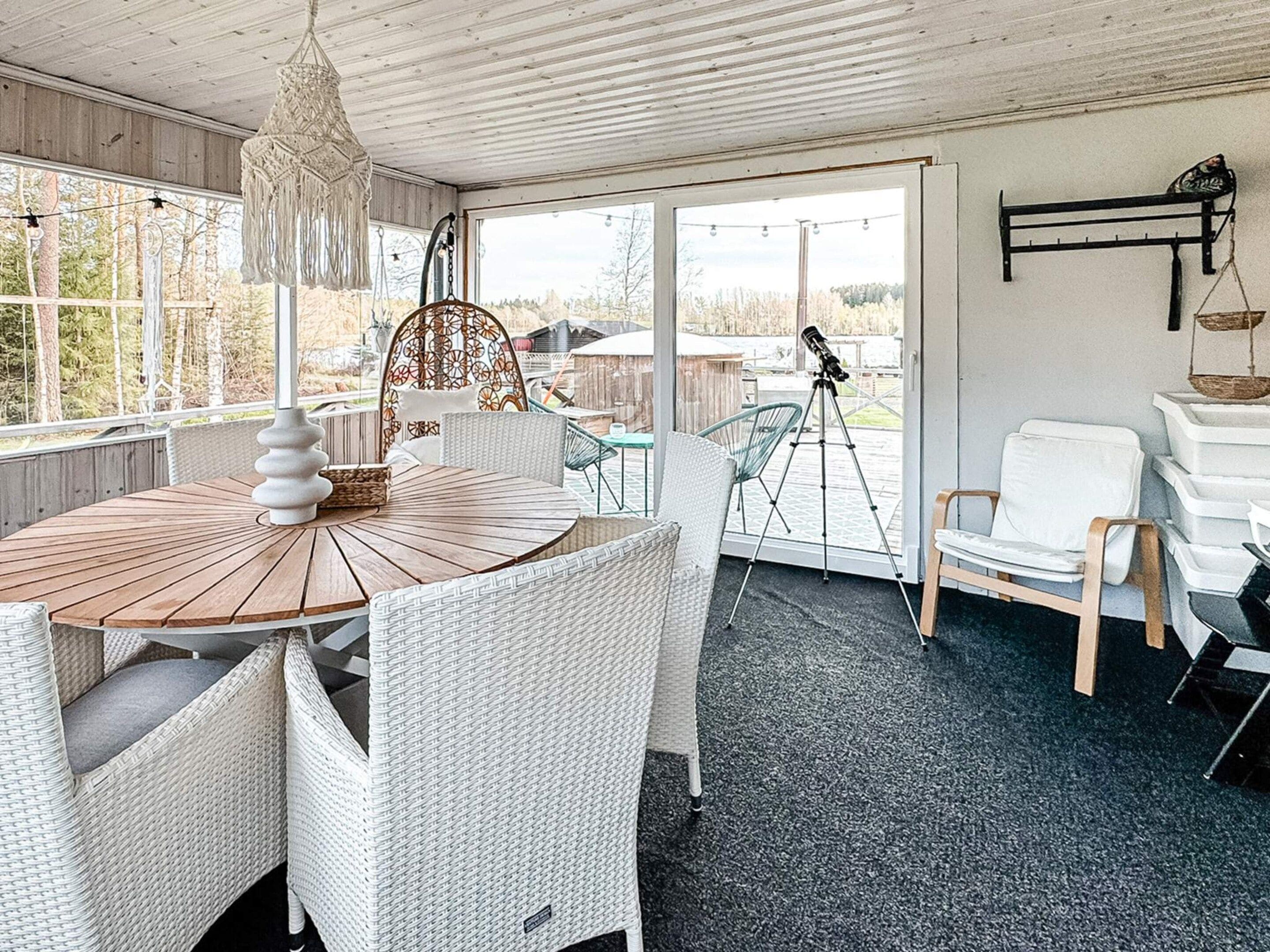 Quarto com mesa redonda de madeira, cadeiras de vime branco, luminária pendente e um telescópio sobre um tripé.
