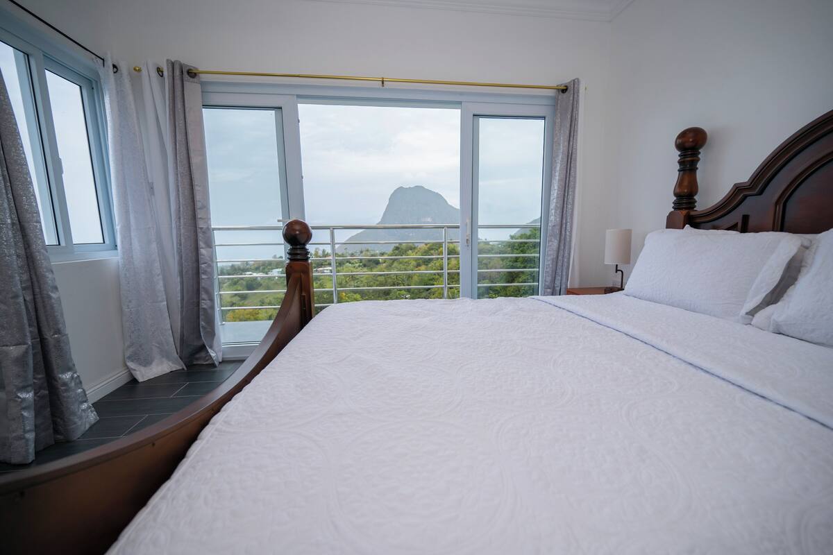 Quarto de hotel com uma cama grande, cabeceira de madeira e varanda com vista para uma montanha.