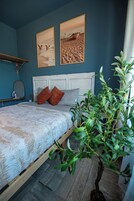 Quarto com cama, planta e duas molduras na parede.
