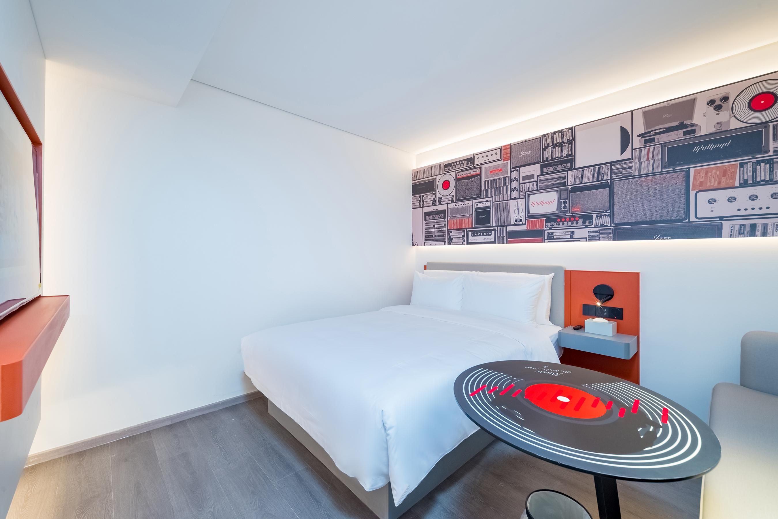 Quarto de hotel moderno com uma cama, toca-discos fixado na parede e obra de arte com diversos equipamentos de áudio.