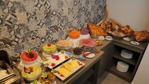 Uma mesa de buffet com diversos alimentos e uma parede de azulejos estampados ao fundo.