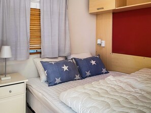 Quarto com cama, travesseiros, mesa de cabeceira, abajur e luminária na parede.