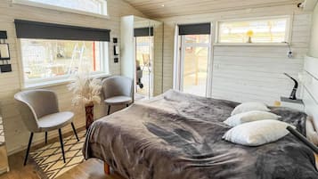 Quarto com cama, duas cadeiras, uma janela e porta que dá para o exterior.