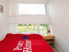 Quarto com cama, janela com cortinas, mesa de cabeceira com abajur e vista para o exterior.