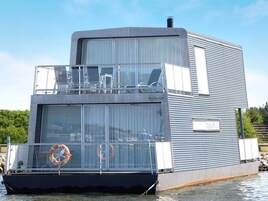 Uma casa barco moderna com teto plano, grandes janelas e uma boia de salvamento na proa.