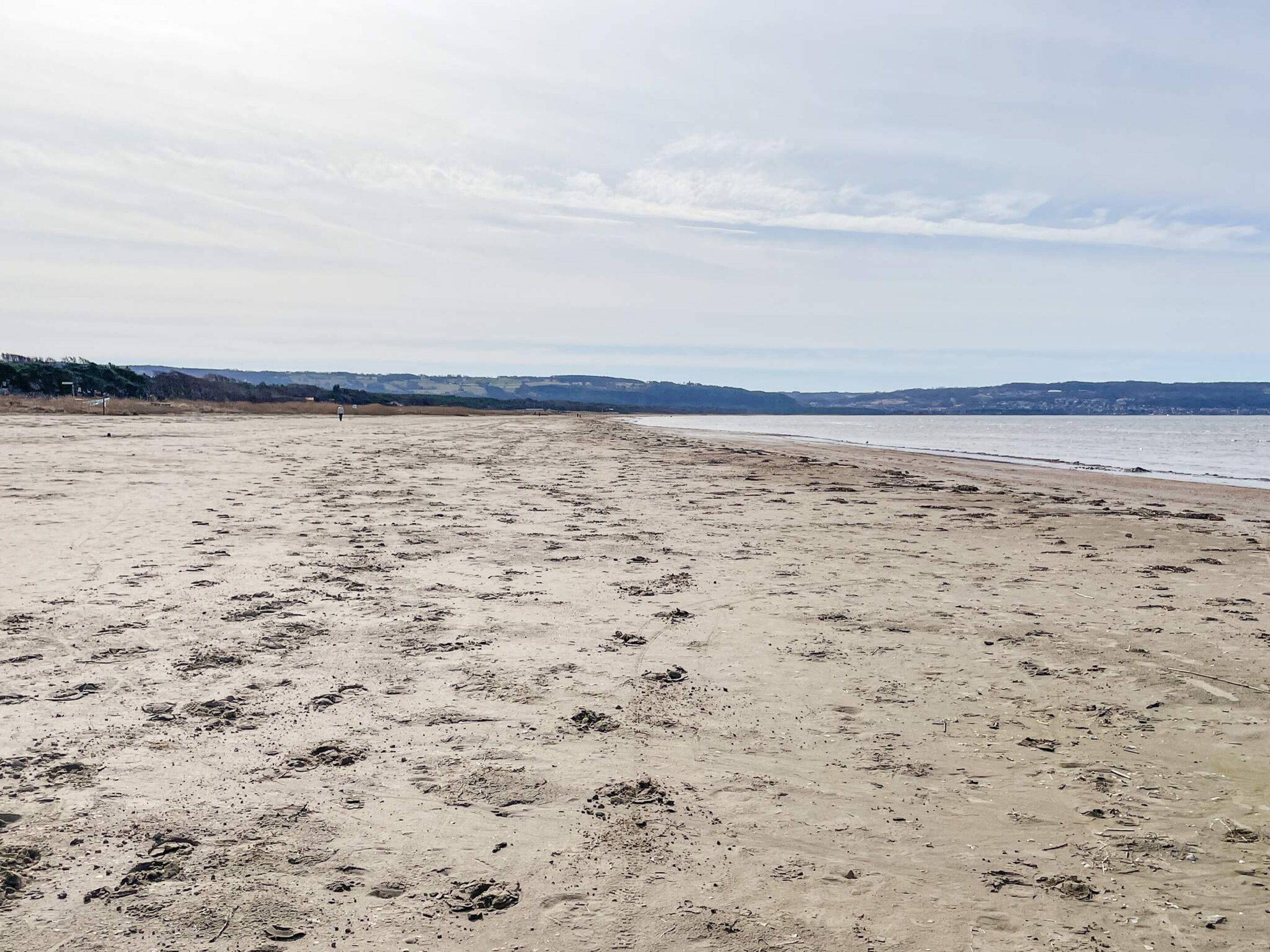 Uma extensa praia de areia com pegadas e mar calmo.