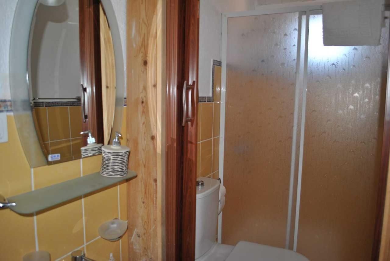 Um banheiro com porta de madeira, vaso sanitário, prateleira com artigos de higiene e um espelho.