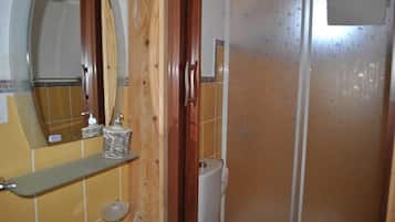 Um banheiro com porta de madeira, vaso sanitário, prateleira com artigos de higiene e um espelho.