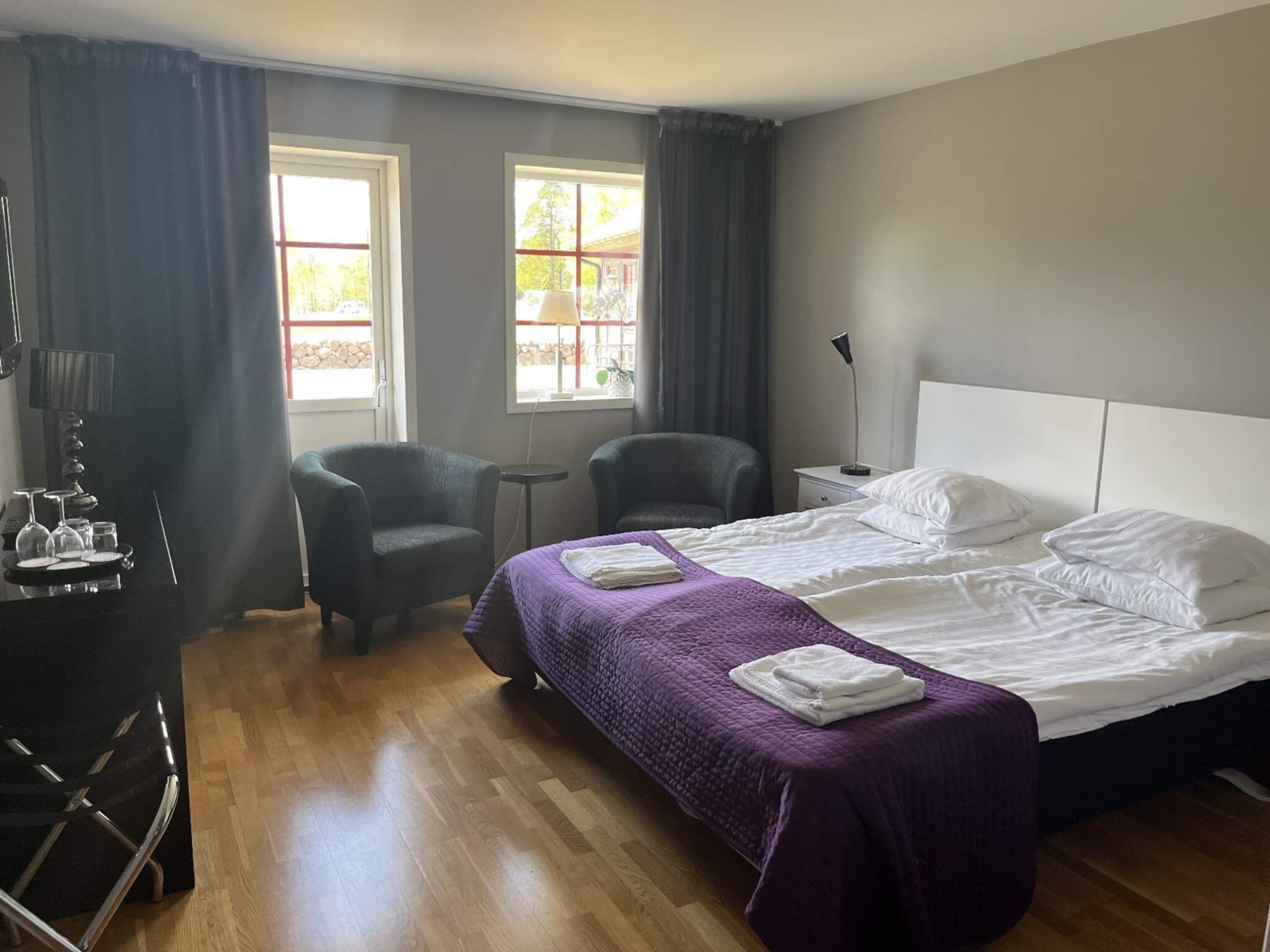 Quarto de hotel com uma cama, duas cadeiras, uma mesinha e uma escrivaninha com abajur.