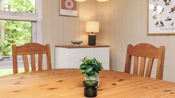 Uma mesa de jantar de madeira com cadeiras, um candeeiro pendente, uma ilustração emoldurada de pássaros e uma pequena planta sobre a mesa.