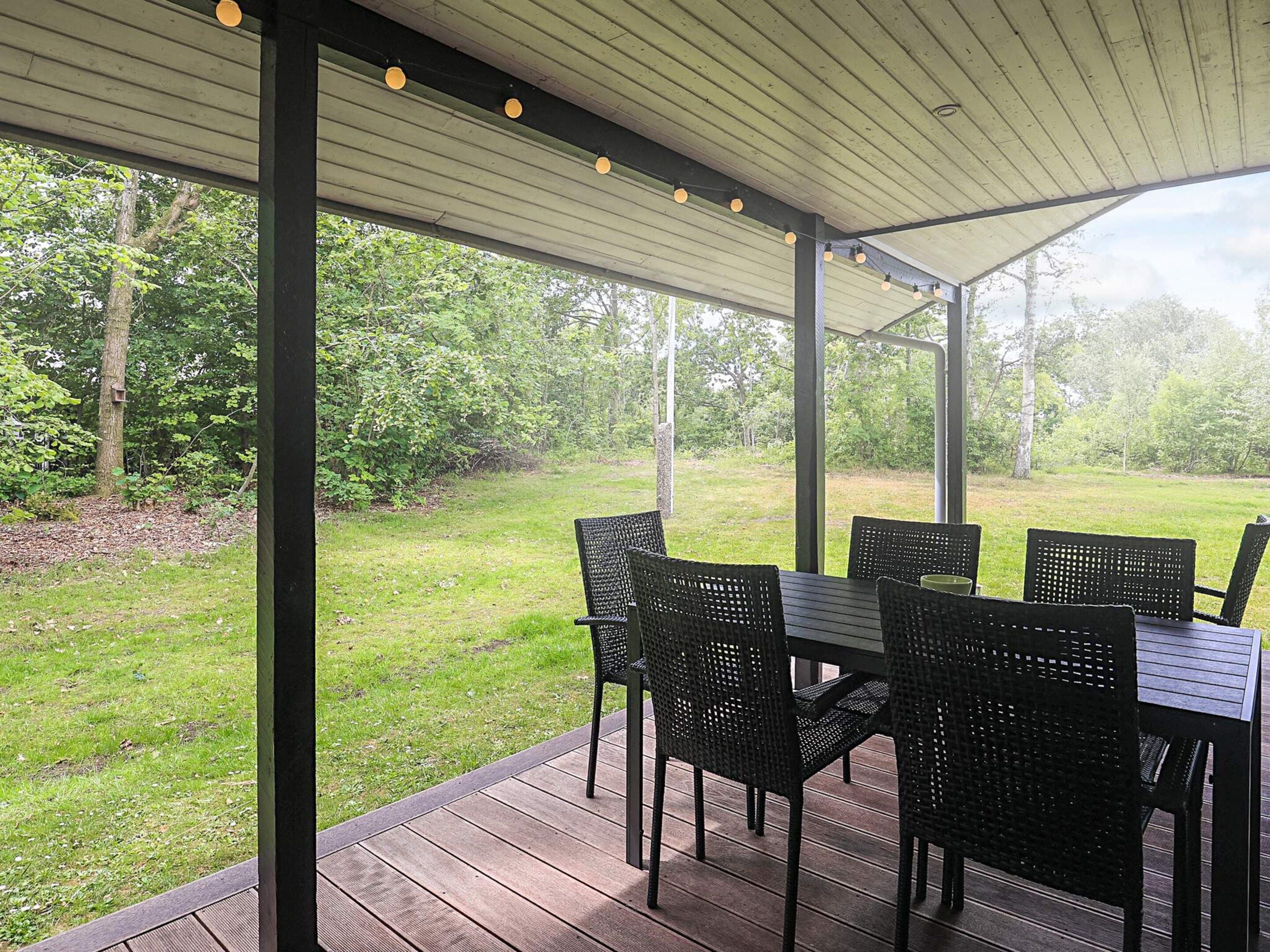 Um pátio externo com mesa e cadeiras, rodeado por um deck de madeira e coberto por um telhado.
