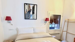 Quarto de hotel com cama, duas luminárias fixadas na parede, um quadro emoldurado, um radiador e uma escada de madeira.