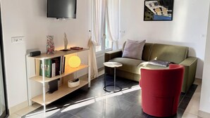 Uma sala de estar moderna com uma TV de tela plana, um sofá verde, um banquinho vermelho e uma mesinha lateral.