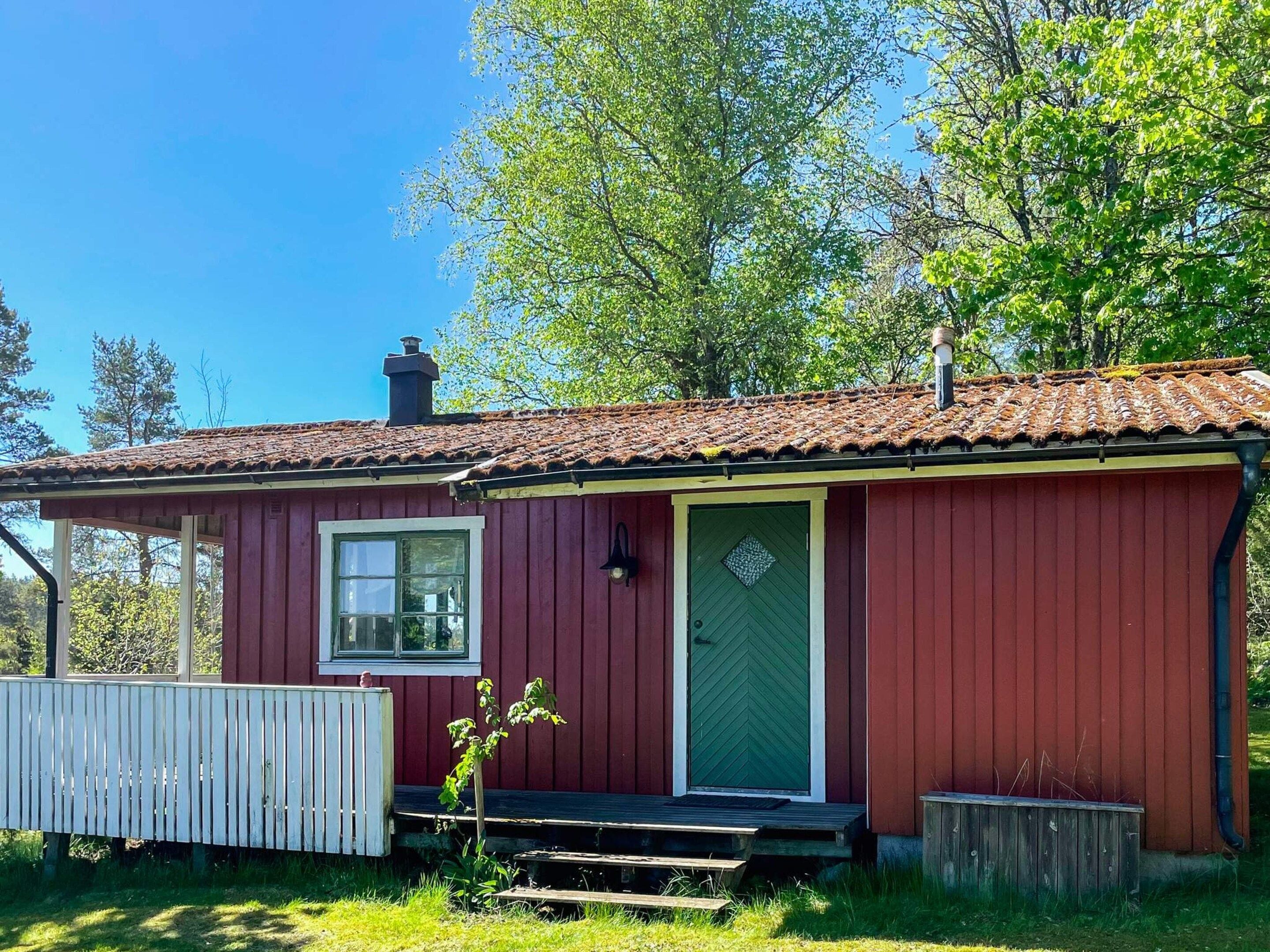 Uma cabana de madeira vermelha com telhado de telhas, porta verde e um pequeno alpendre.